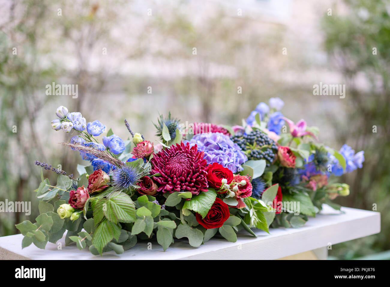 Elongated floral arrangement in vintage metal vase. table setting. Blue ...