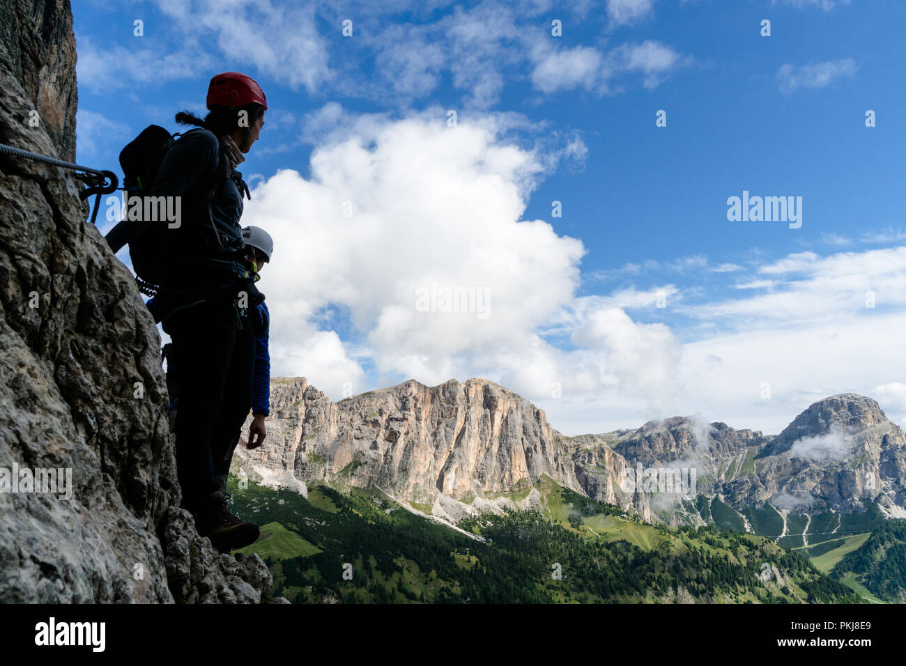 two young mountain climbers in silhouette on a steep and exposed climb ...