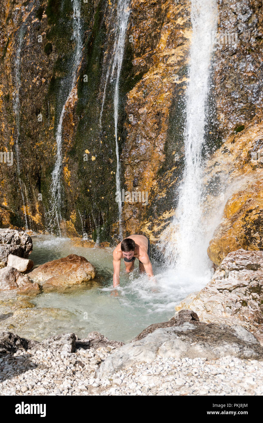 young athletic male goes for a refreshing bath in a mountain waterfall ...