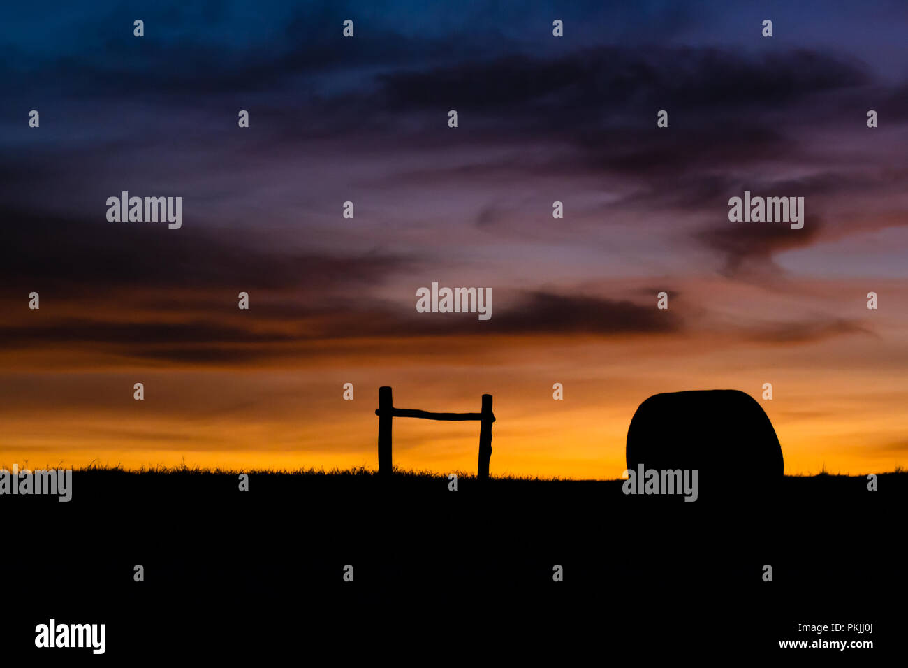 sunset landscape with fence post & hay bail silhouette Stock Photo - Alamy