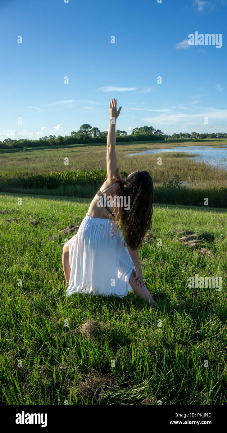 Young brunette spanish woman doing reverse warrior yoga pose in a field ...