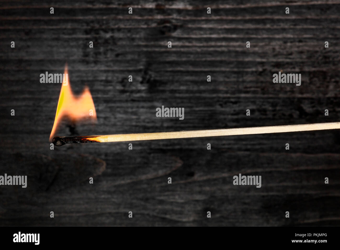 A side view of a burning match, with fire, on a dark background with ...