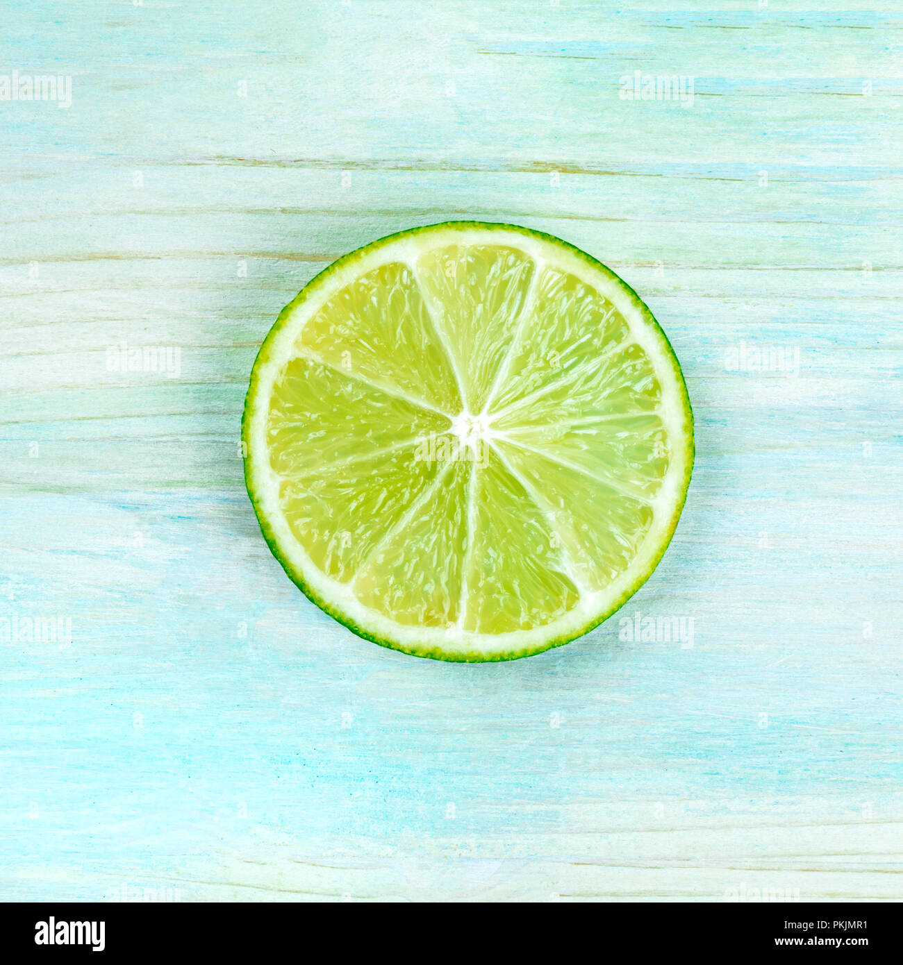 An overhead photo of a single lime slice on a teal blue background ...