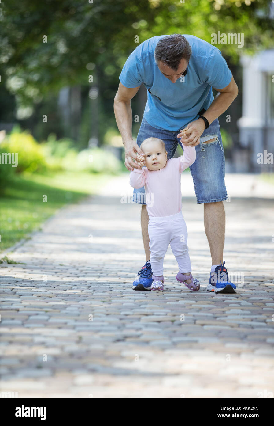 Father supporting baby daughter and helping her make first steps. Dad ...