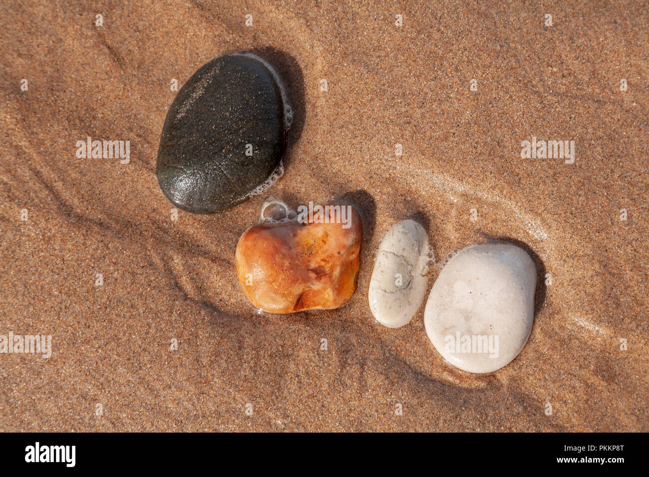 Smooth wet stones in the sand on the Antrim coast at Whitepark Bay ...