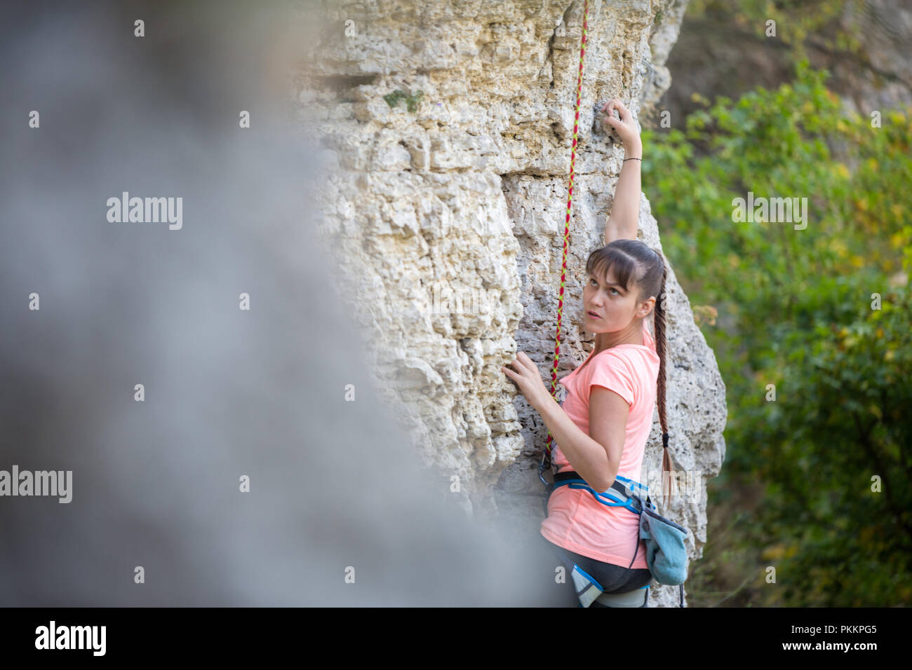 Photo of athlete girl clambering over rock against background of green ...