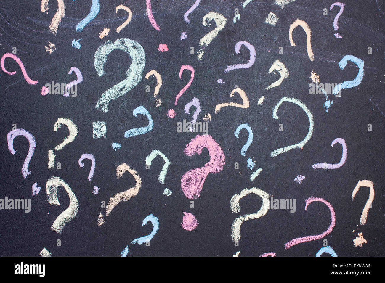 Multicolored question marks are painted with chalk on a blackboard ...