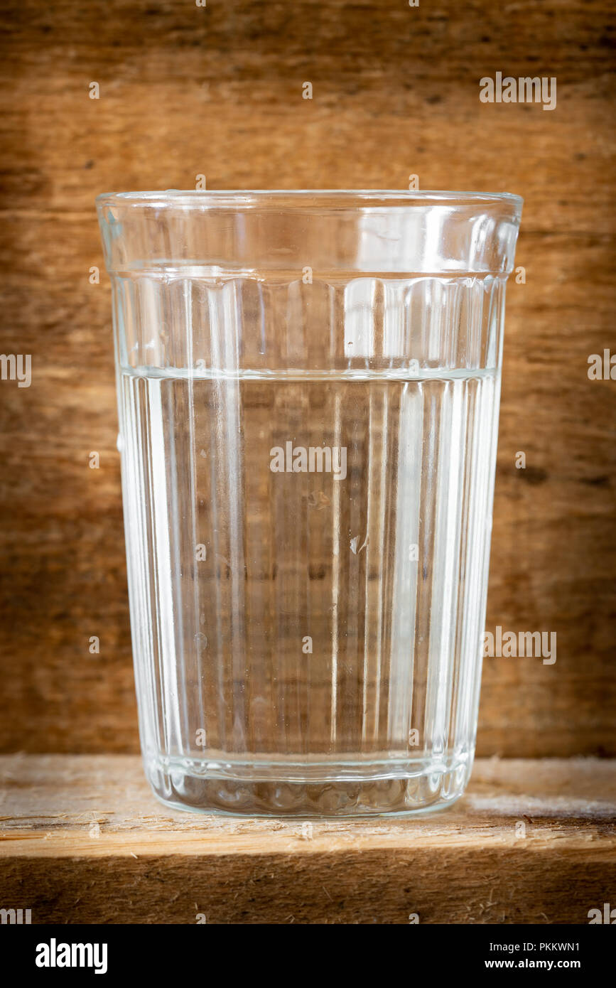 One glass of water, illuminated with natural light, on a wooden plank ...