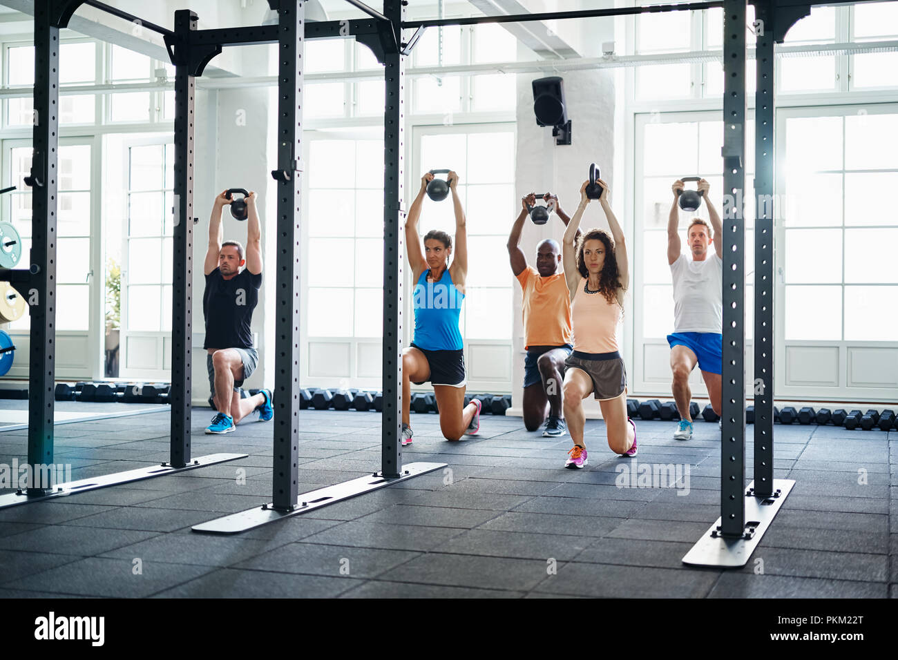 Diverse group of young people doing lunges with weights in a gym ...