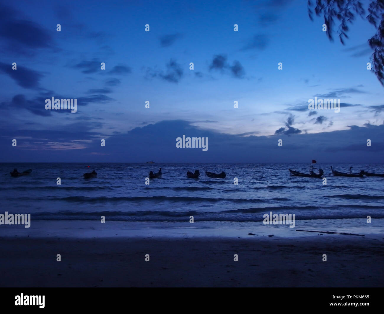 Evening dusk shot of the sea in the blue hour with silohettes of boats ...
