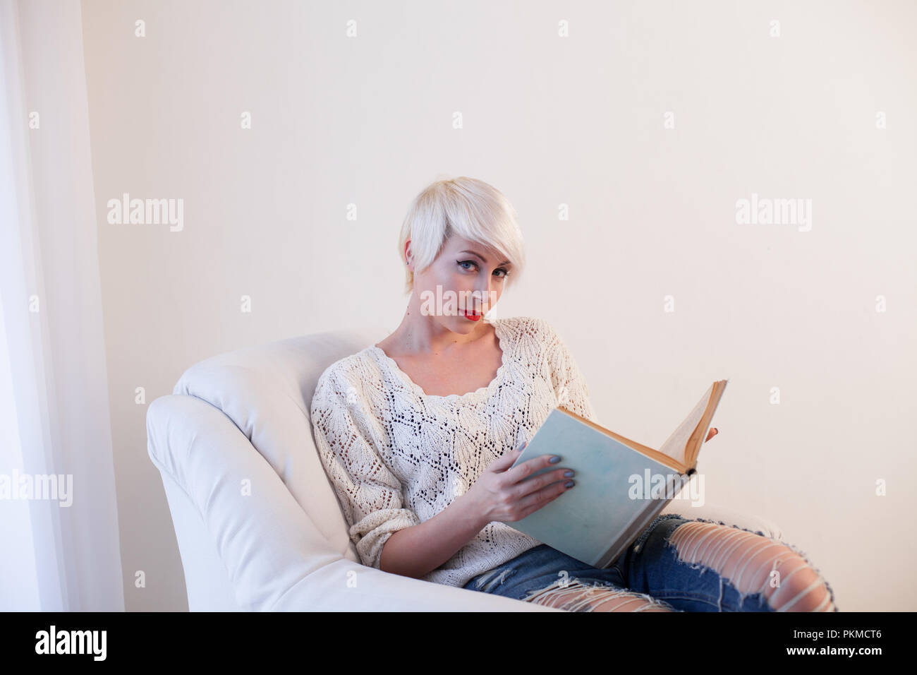 woman reading a book in a Chair in a white room Stock Photo - Alamy