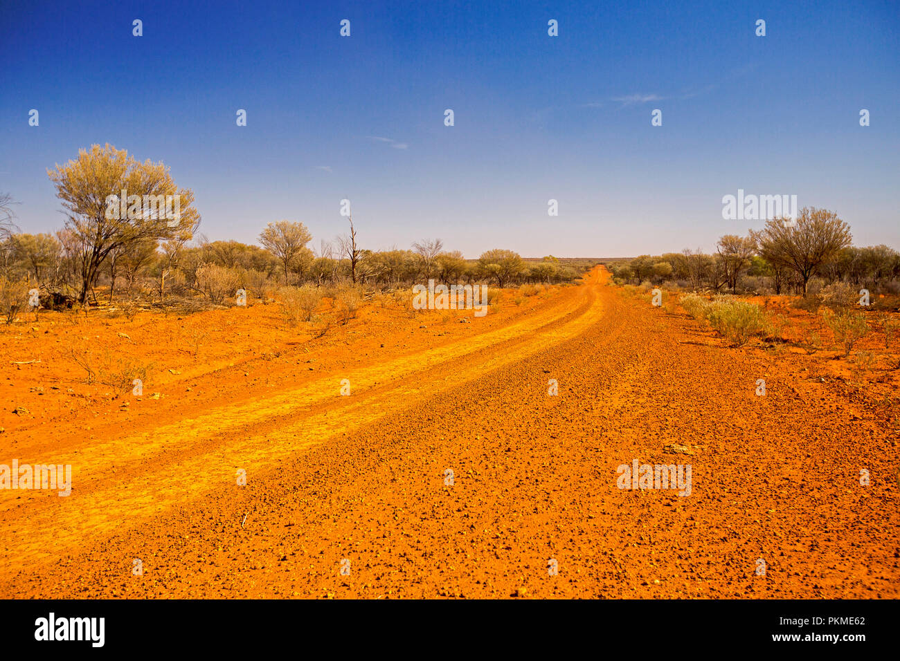 Red Australian outback road slicing through arid landscape cloaked with ...