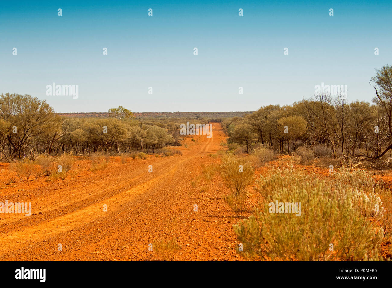 Red Australian outback road slicing through arid landscape cloaked with ...