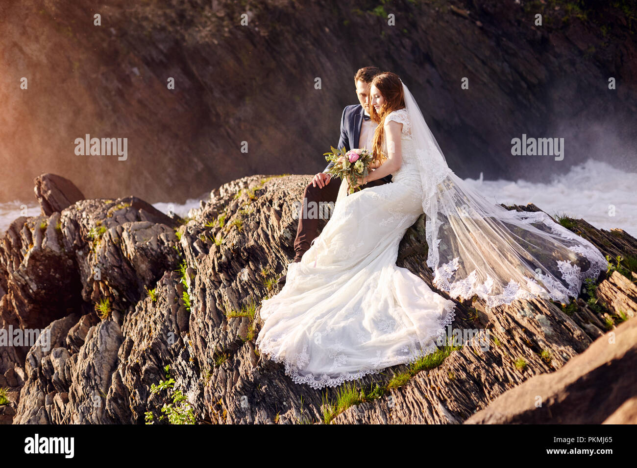 Beautiful couple in love kissing while sitting on the rocks near sea ...