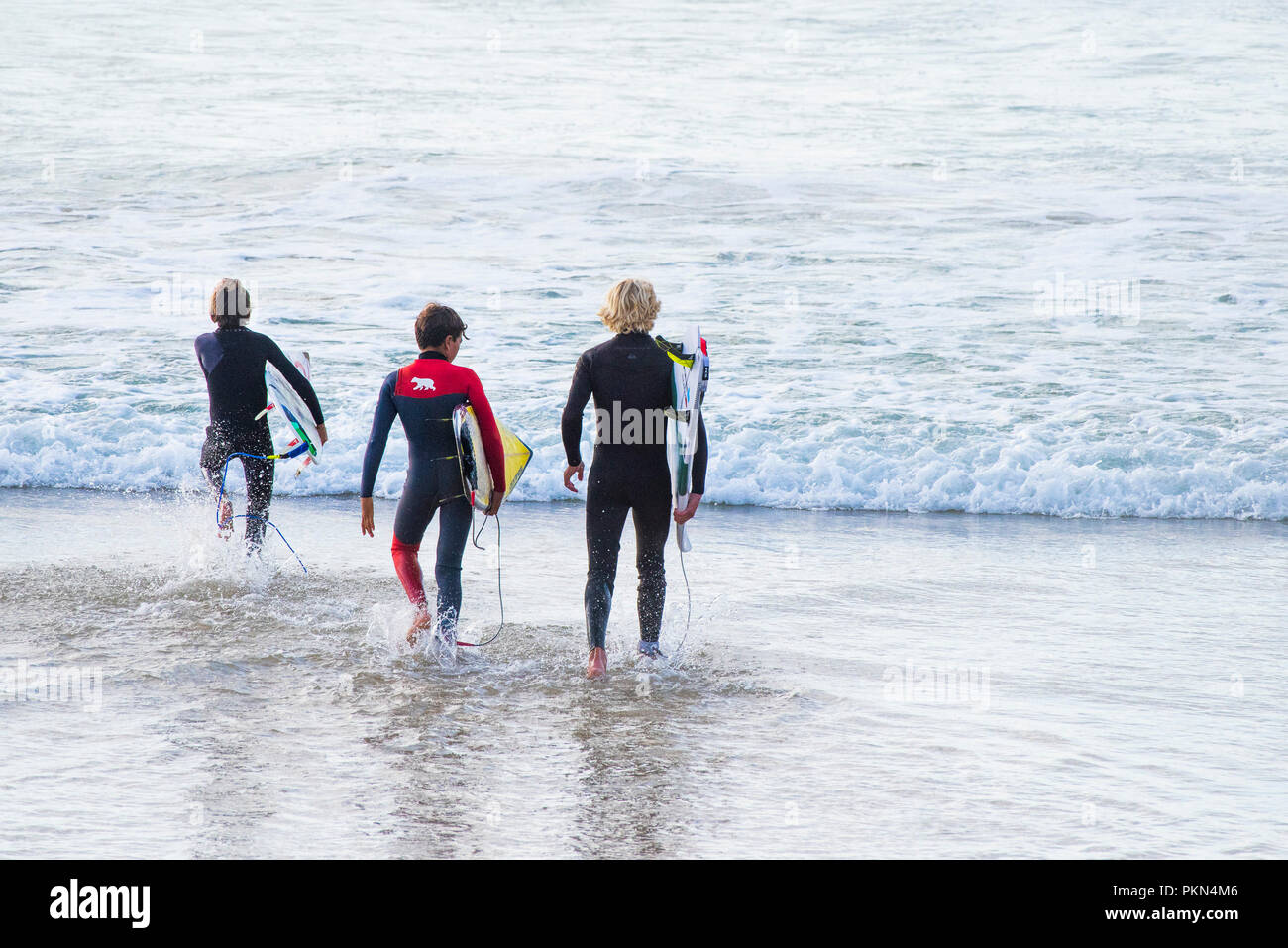 Three young surfers carrying their surfboards and running into the sea ...