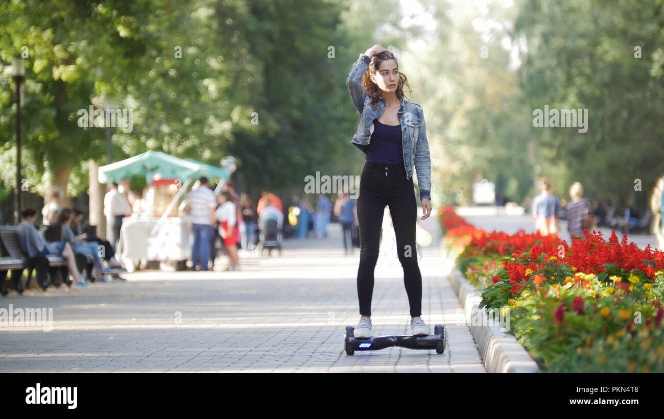 Girl riding a gyro in the park, looking to the side, straightens her ...