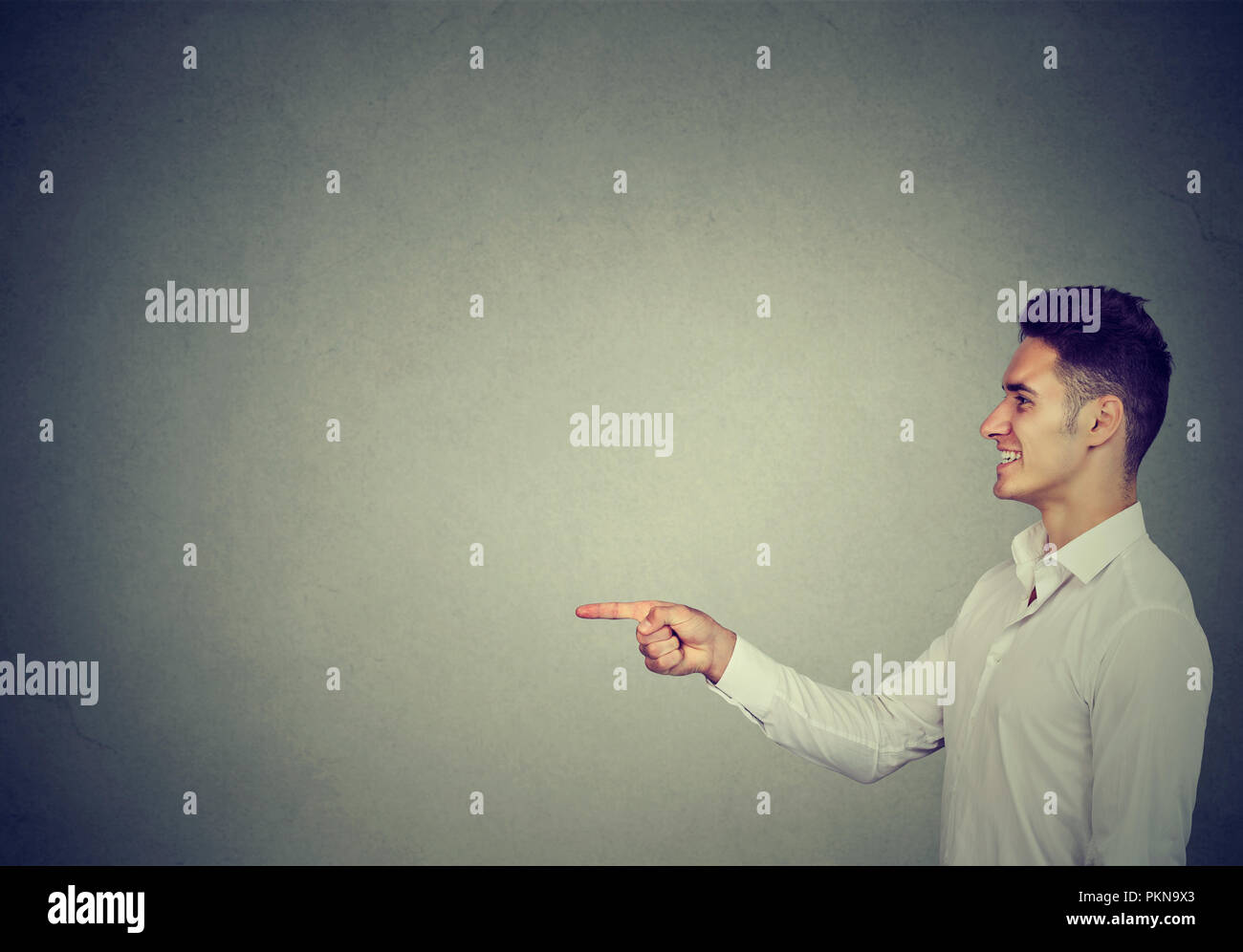 Side view of young smiling man pointing away looking happy on gray ...
