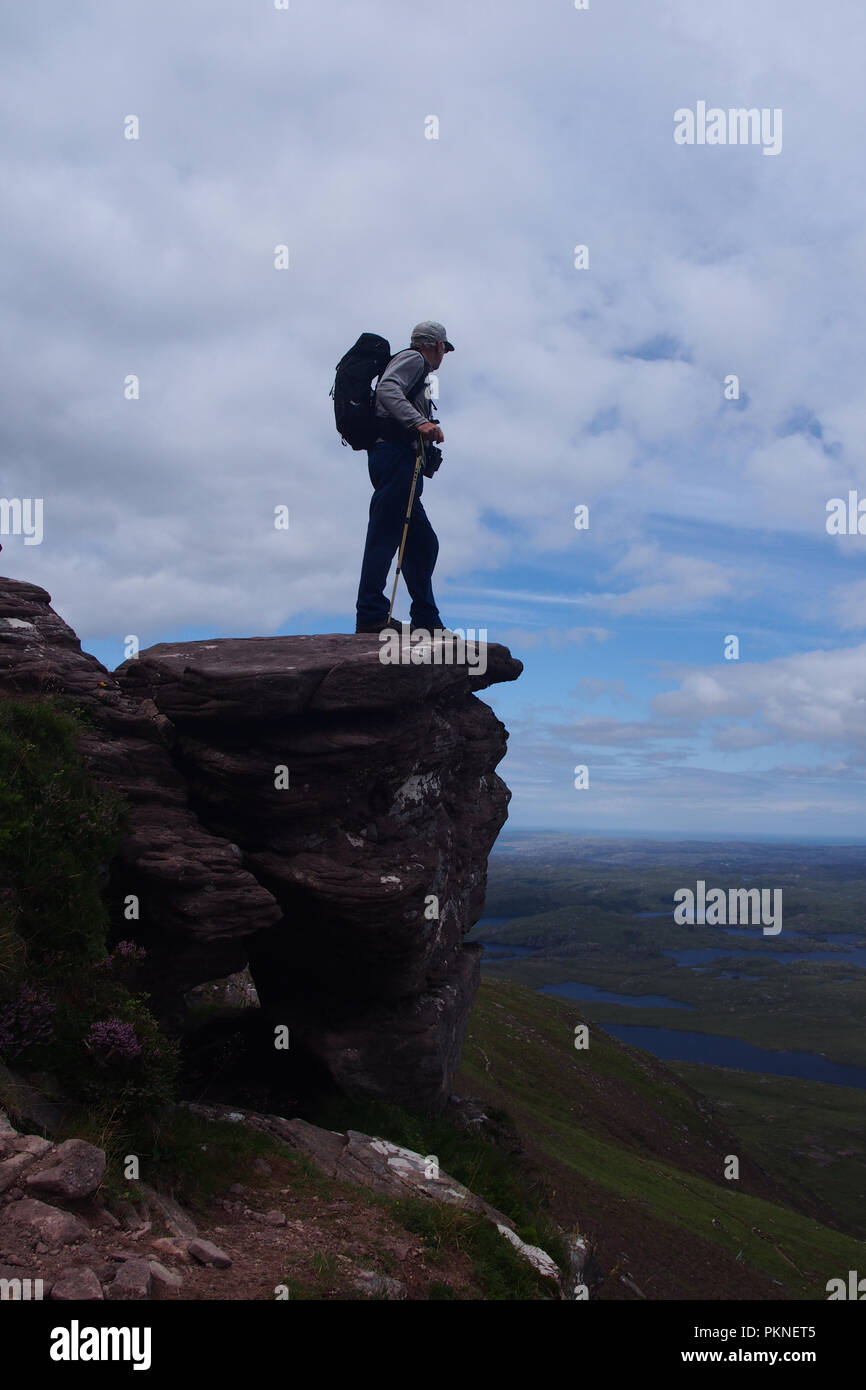 A man in his sixties standing on a rocky ledge half way up a mountain ...