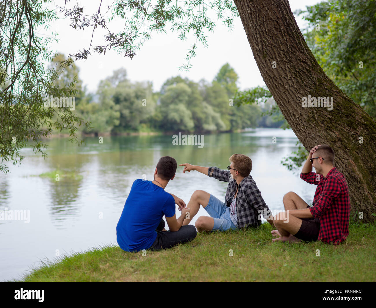 Group of young men enjoying the nature sitting on the bank of the river ...