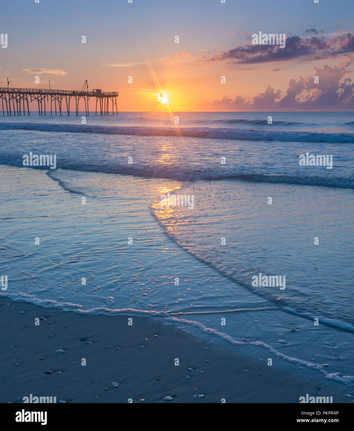 A wooden pier in the ocean with the sun on the horizon taken along the ...