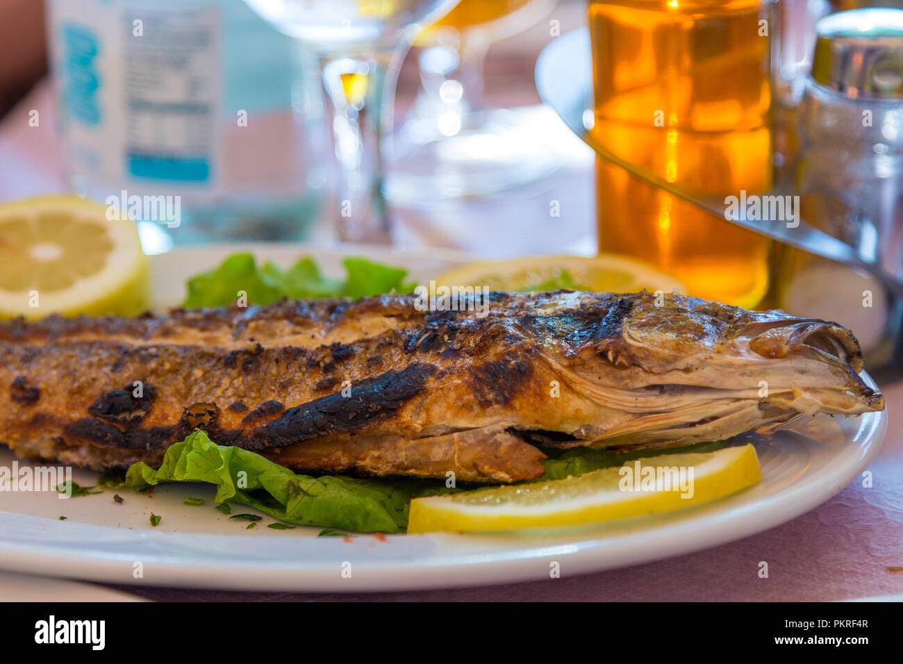 Grilled sea fish a white plate with lettuce and lemon. Restaurant in ...