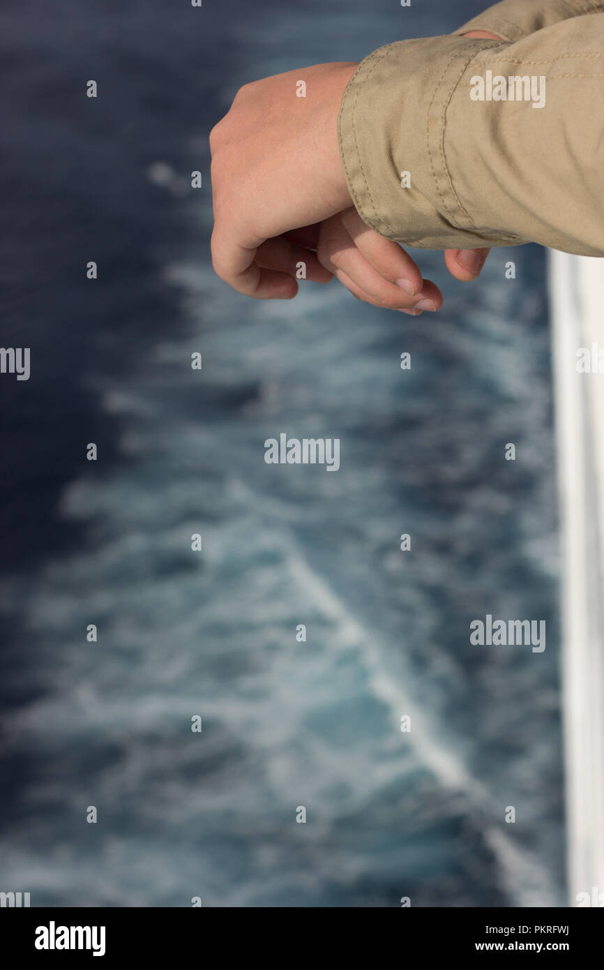 The joined hands of a traveler stand over the foamy waters on the deck ...