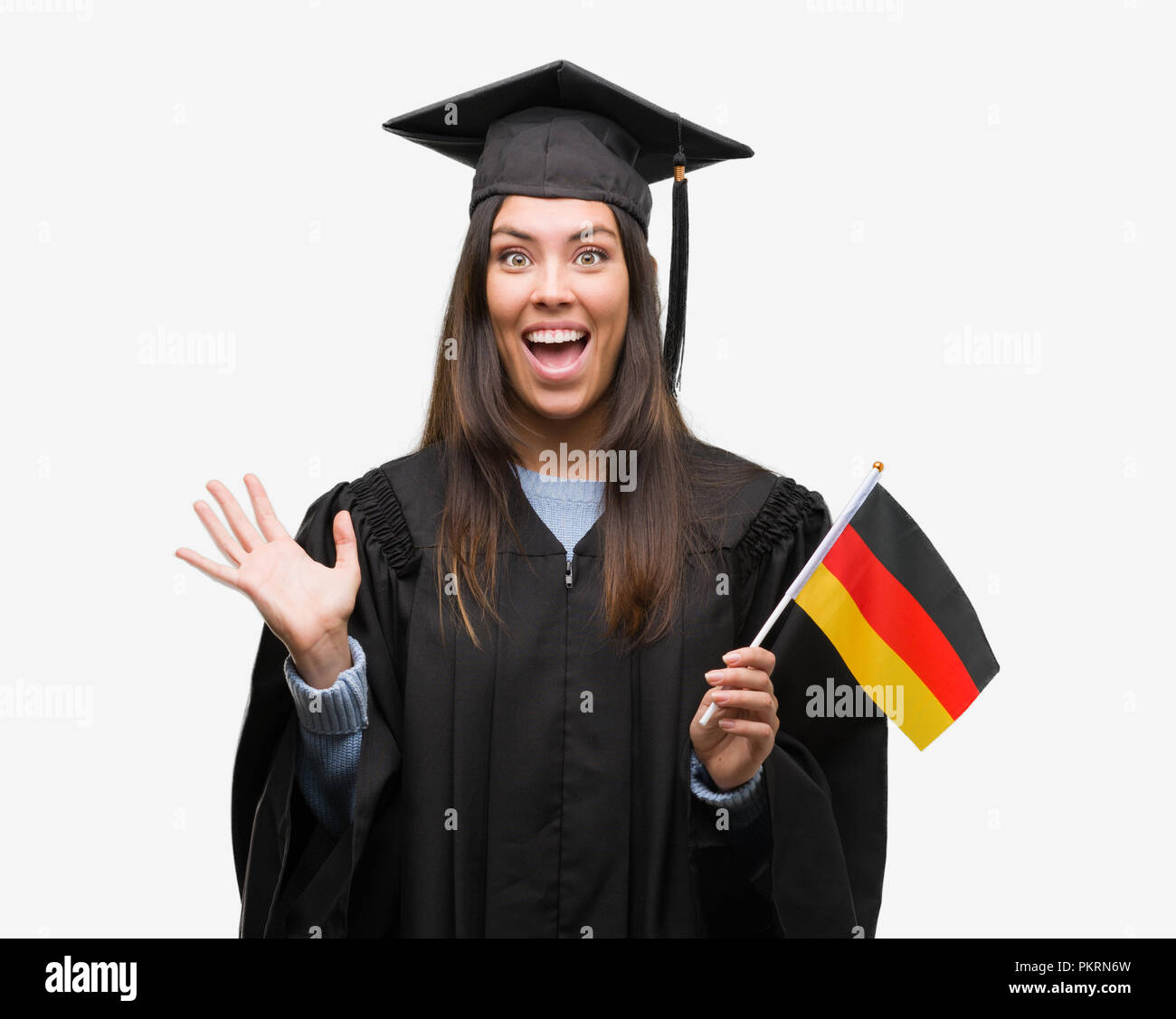 Young hispanic woman wearing graduated uniform holding flag of germany ...