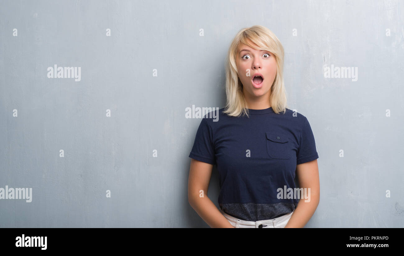 Adult caucasian woman over grunge grey wall scared in shock with a ...