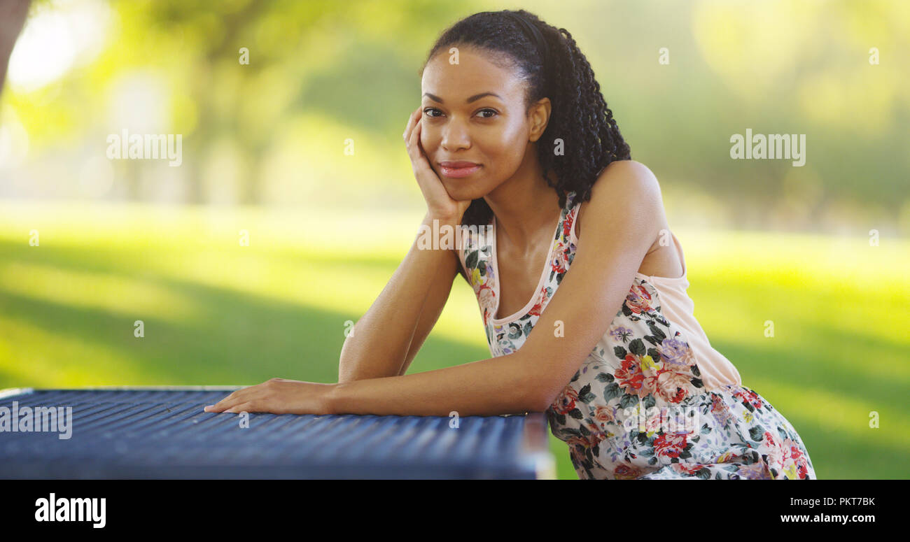 Black woman sitting on a park bench smiling Stock Photo - Alamy