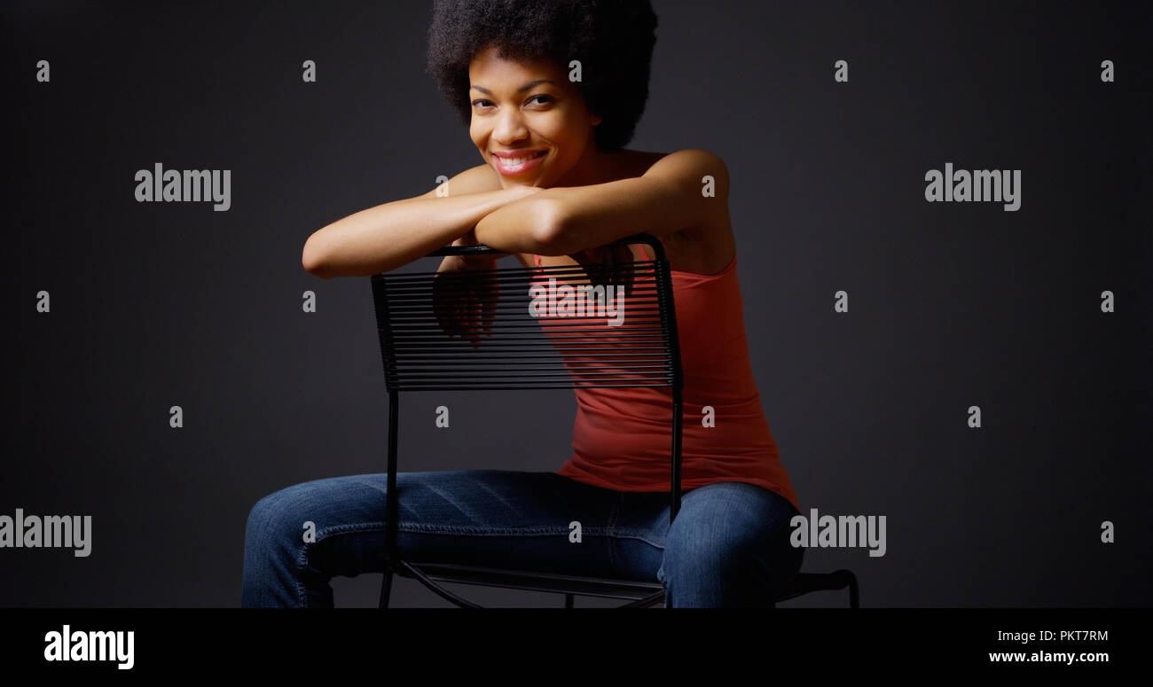 Smiling black woman sitting with arms over back of chair Stock Photo ...