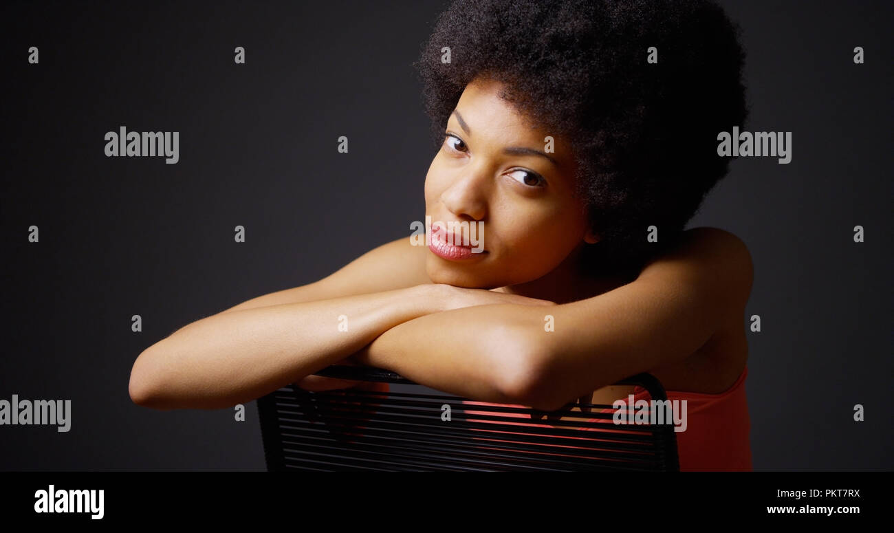 Smiling black woman sitting with arms over back of chair Stock Photo ...