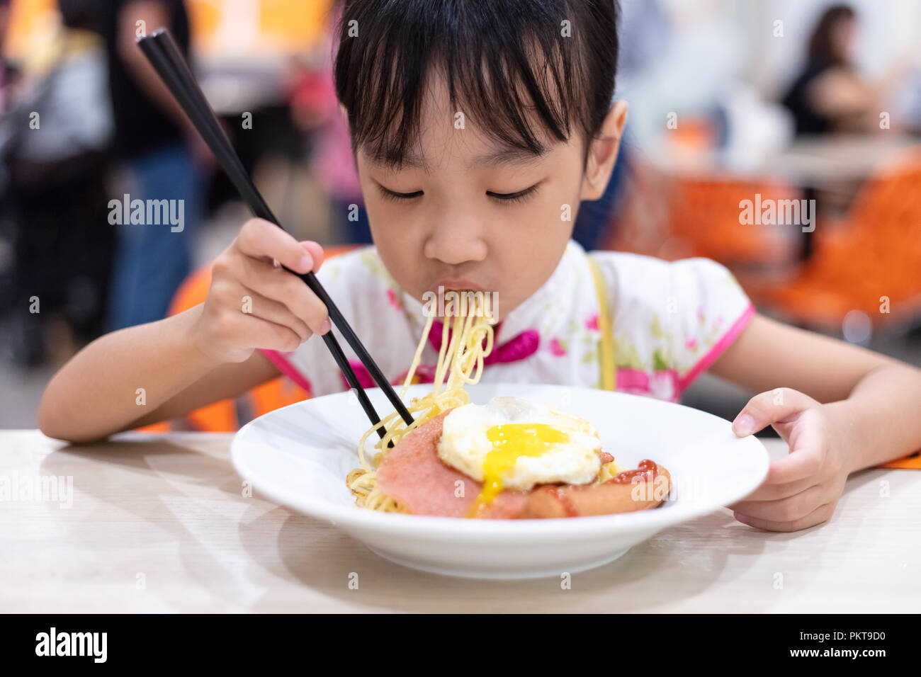 Asian Chinese little girl eating noodles with chopsticks in restaurant ...