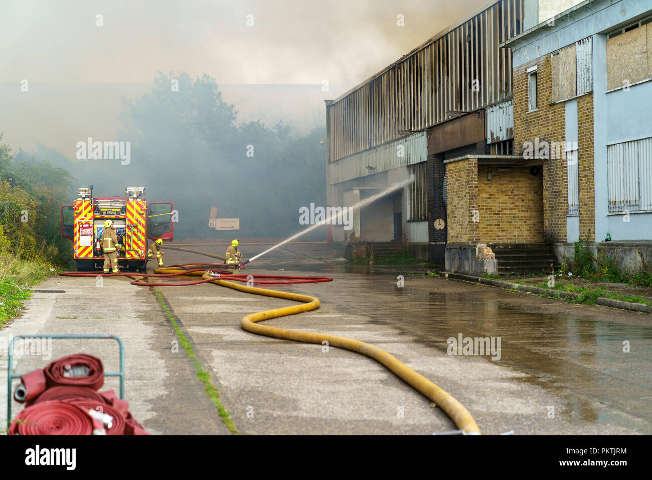 Firemen operating water hose directed at open windows of factory on ...