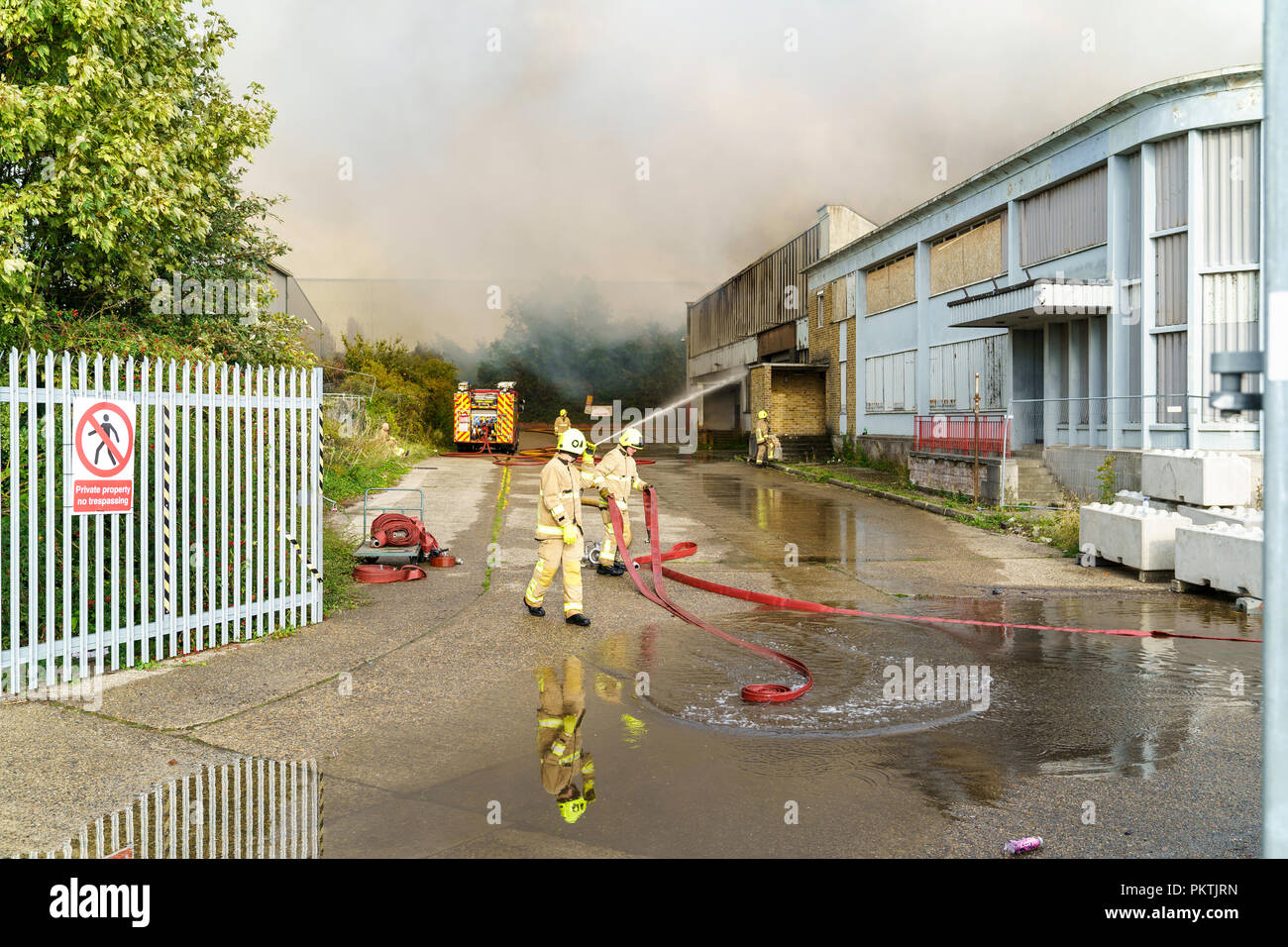 Firemen operating water hose directed at open windows of factory on ...