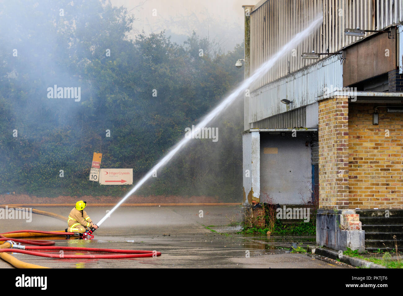Firemen operating water hose directed at open windows of factory on ...
