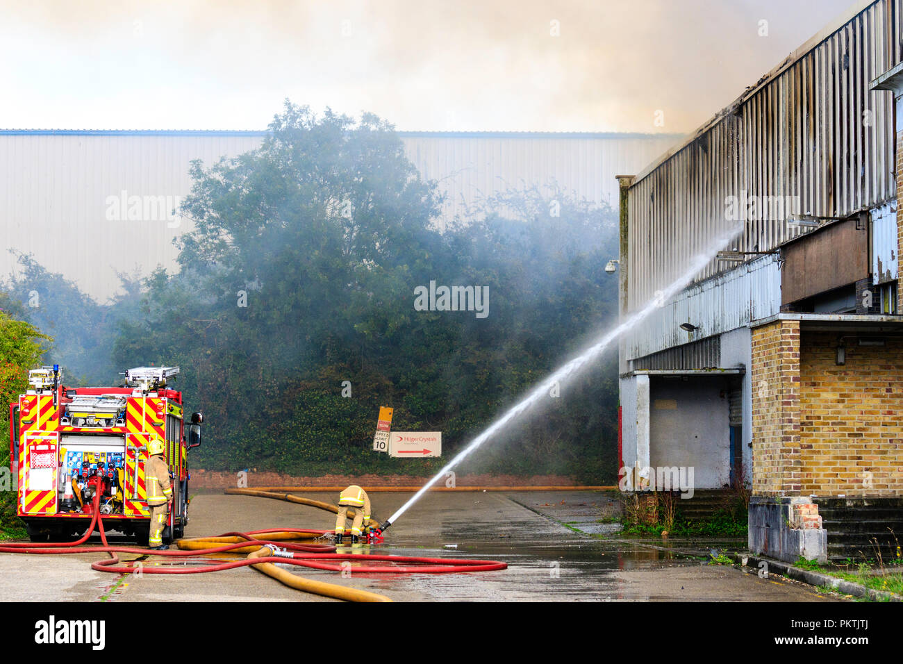 Firemen operating water hose directed at open windows of factory on ...