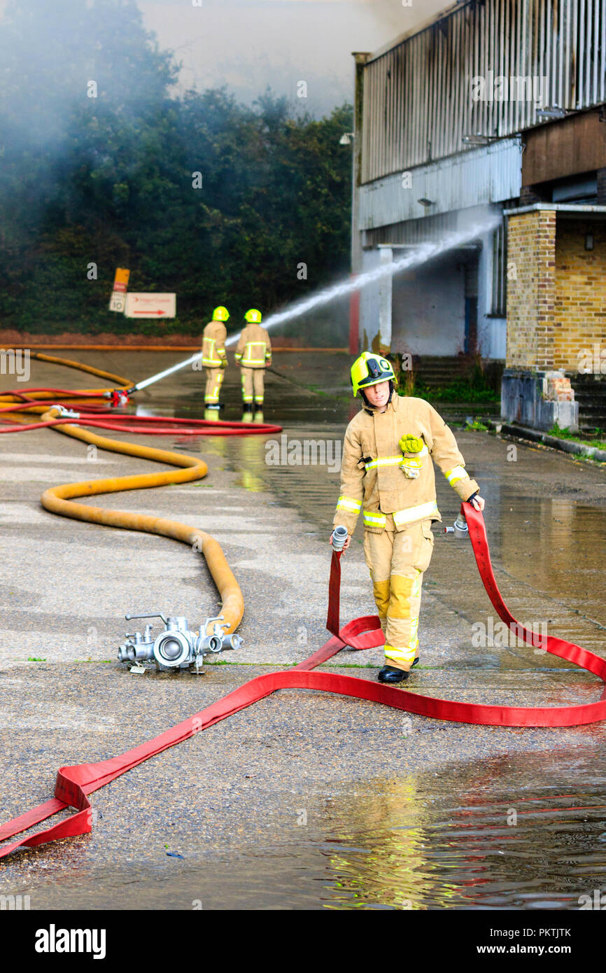 Firemen operating water hose directed at open windows of factory on ...