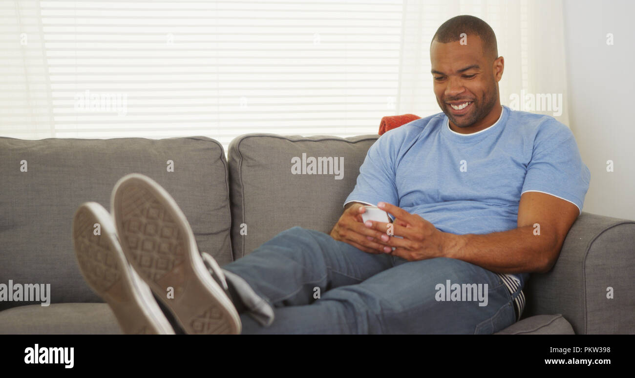 Black man sitting on couch texting Stock Photo - Alamy