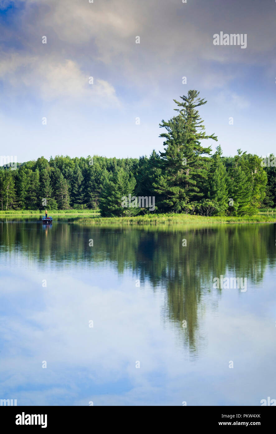 A man stands in a boat fishing on a clear, calm Minnesota lake Stock ...