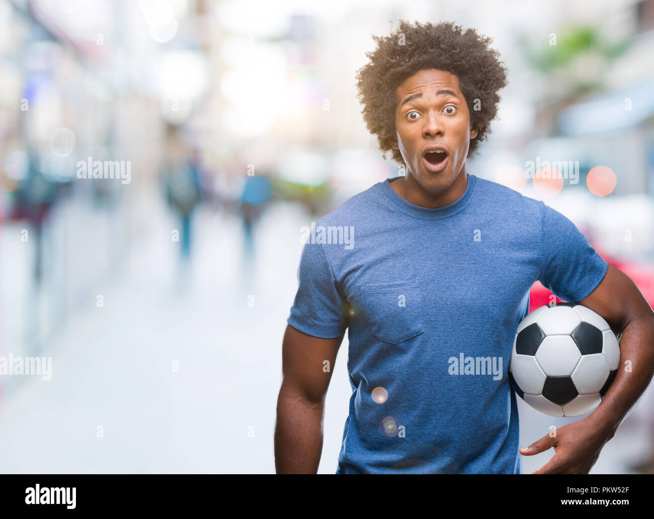 Afro american man holding football ball over isolated background scared ...