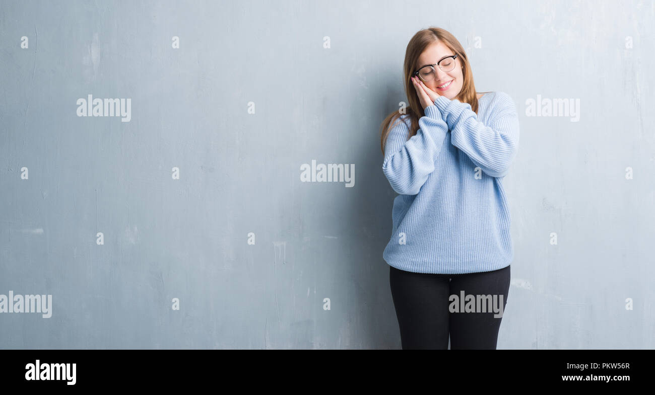 Young adult woman over grey grunge wall wearing glasses sleeping tired ...