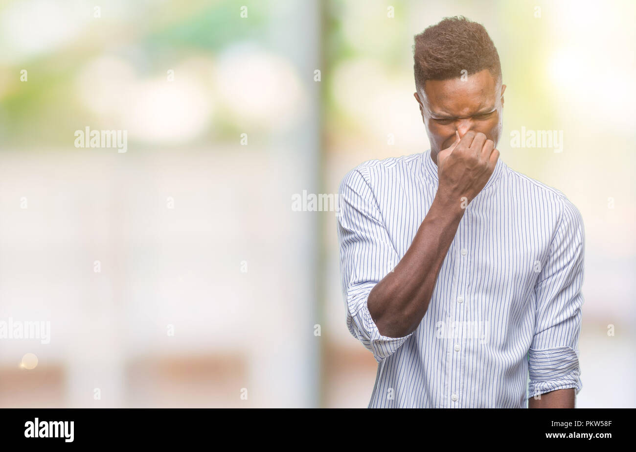 Young african american man over isolated background smelling something ...