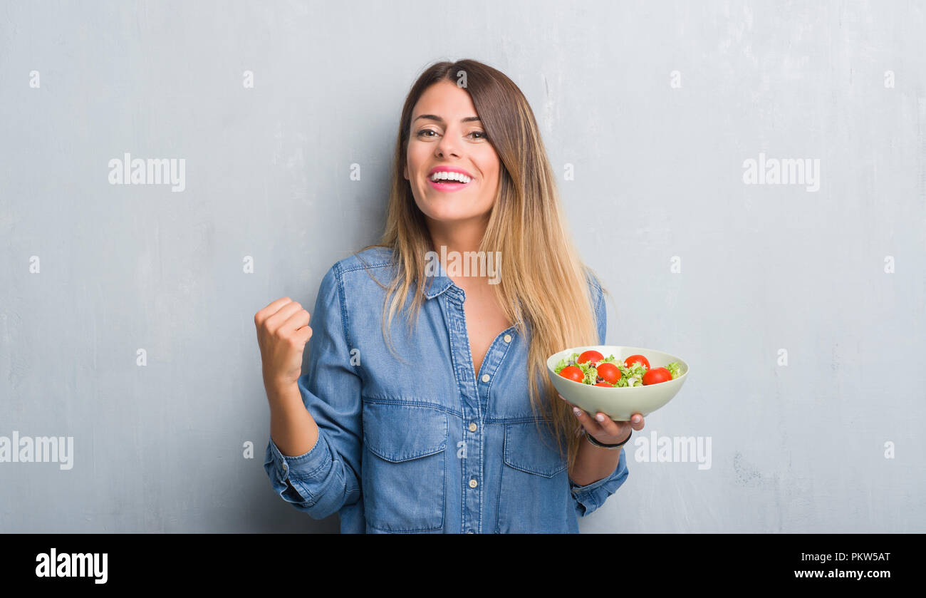 Young adult woman over grey grunge wall eating healthy tomato salad ...