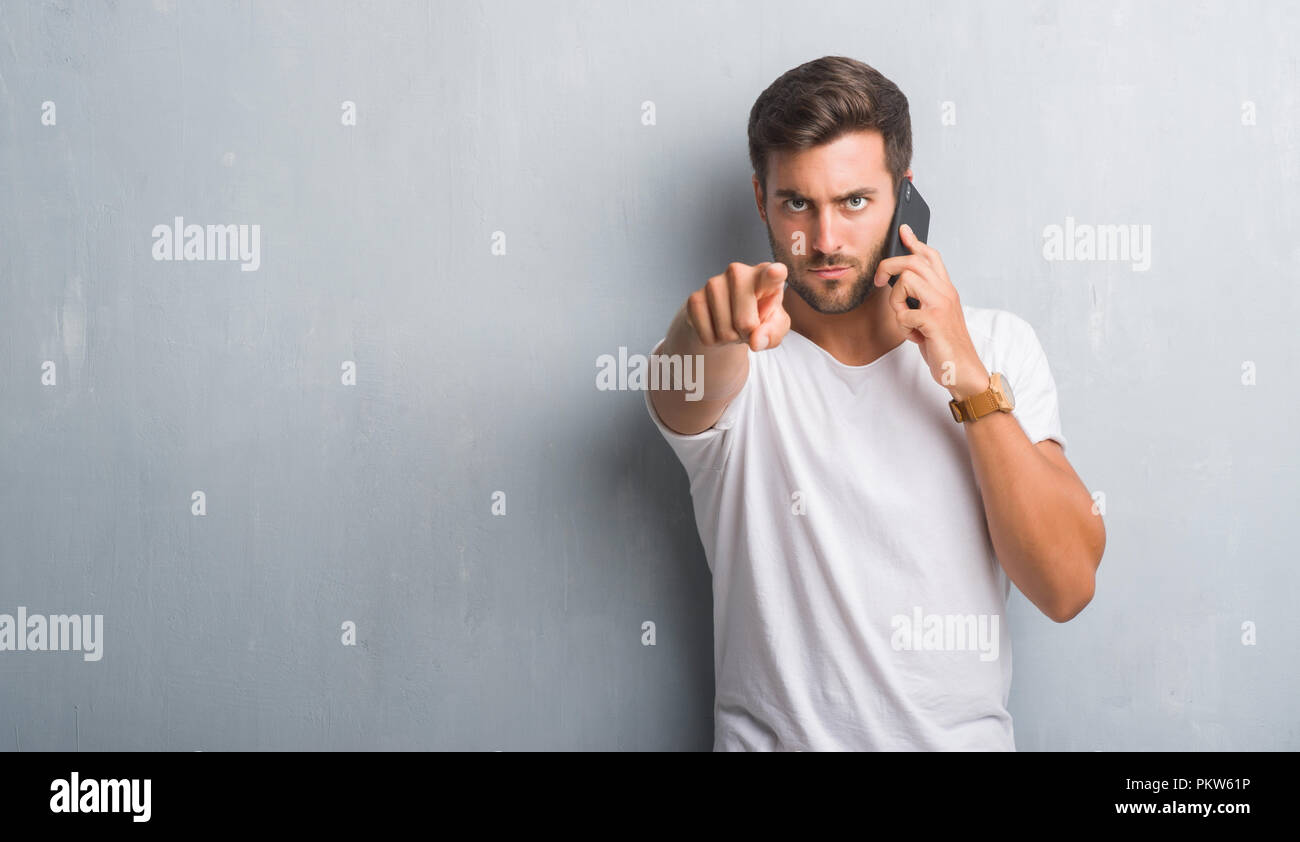 Handsome young man over grey grunge wall speaking on the phone pointing ...