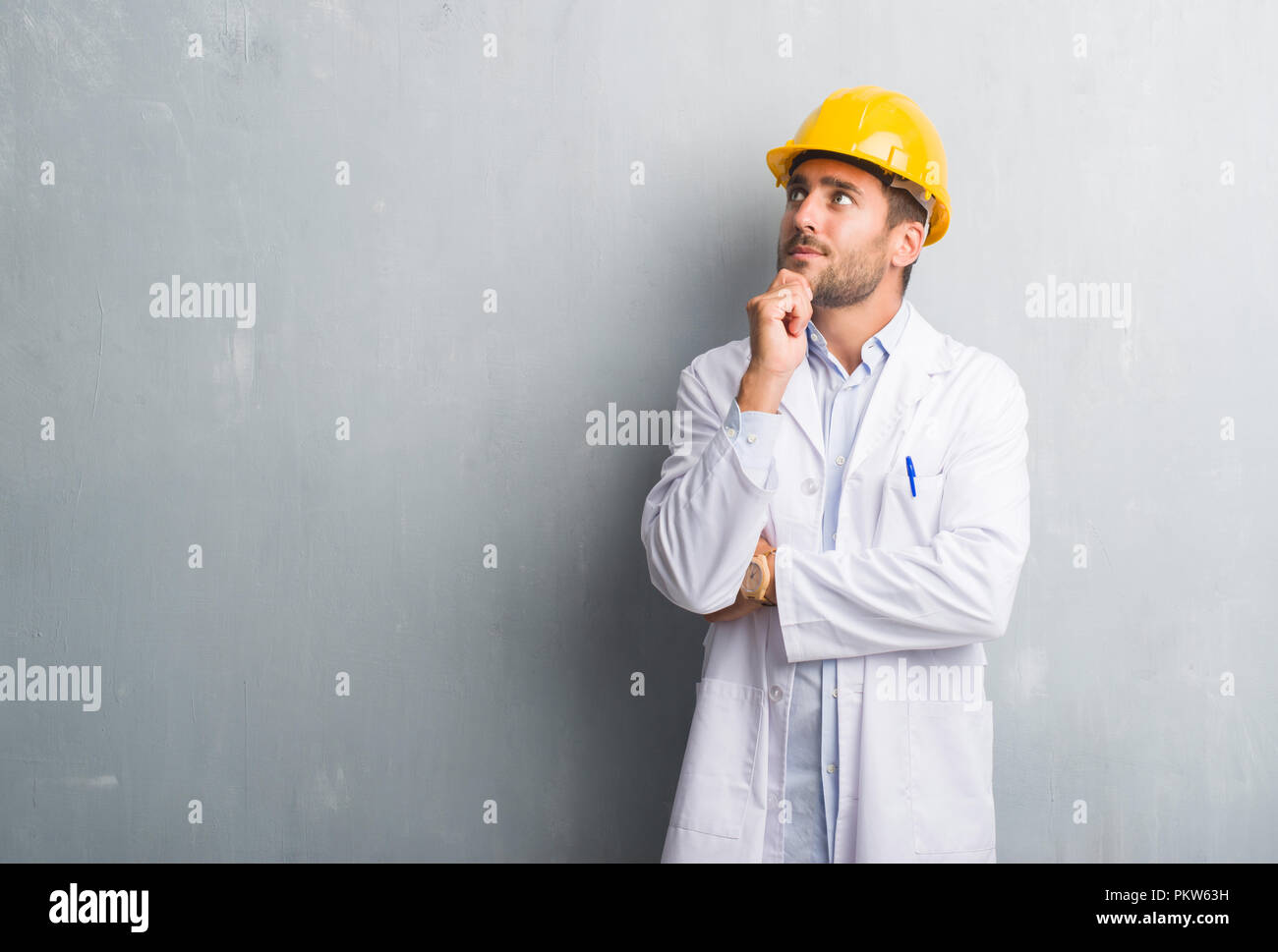 Handsome young engineer man over grey grunge wall wearing safety helmet ...