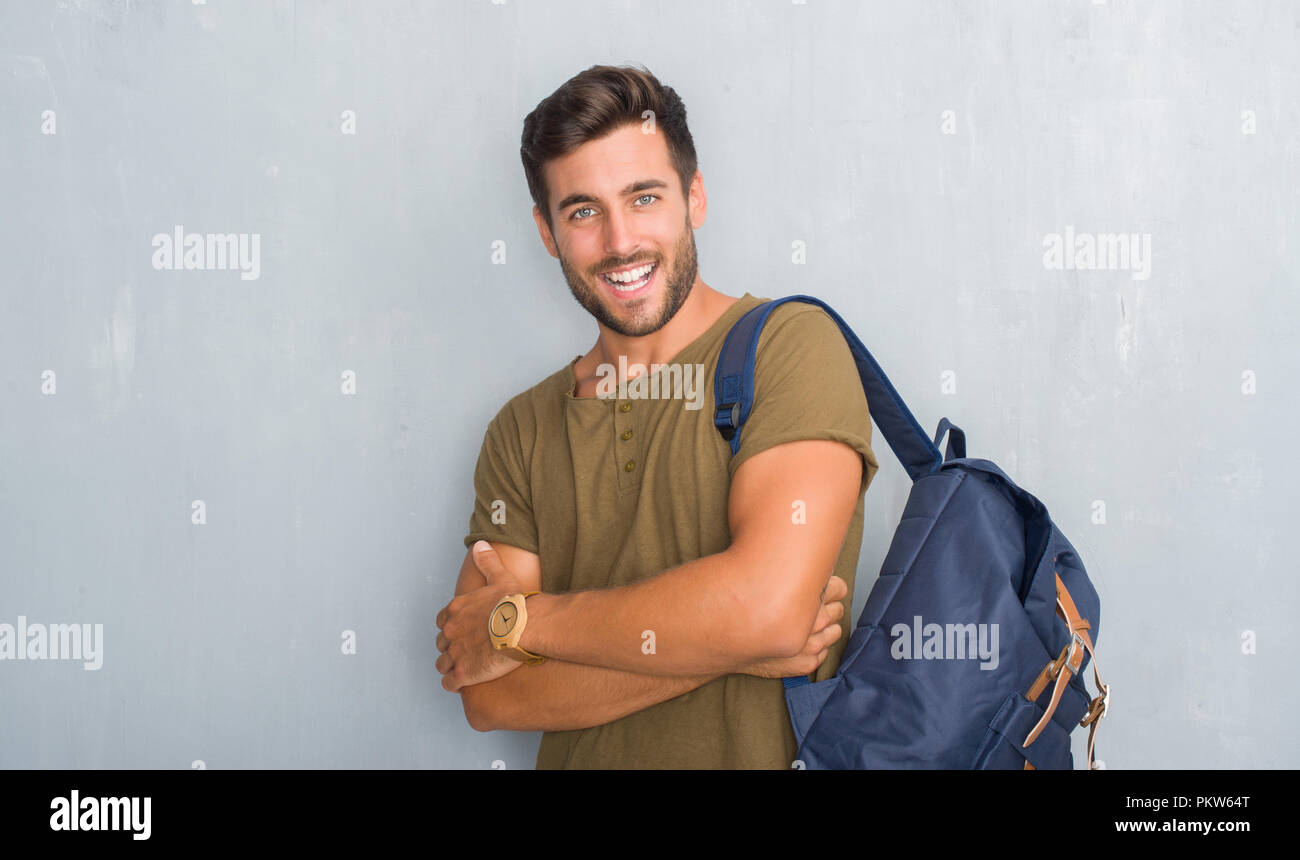 Handsome tourist young man over grey grunge wall wearing backpack happy ...