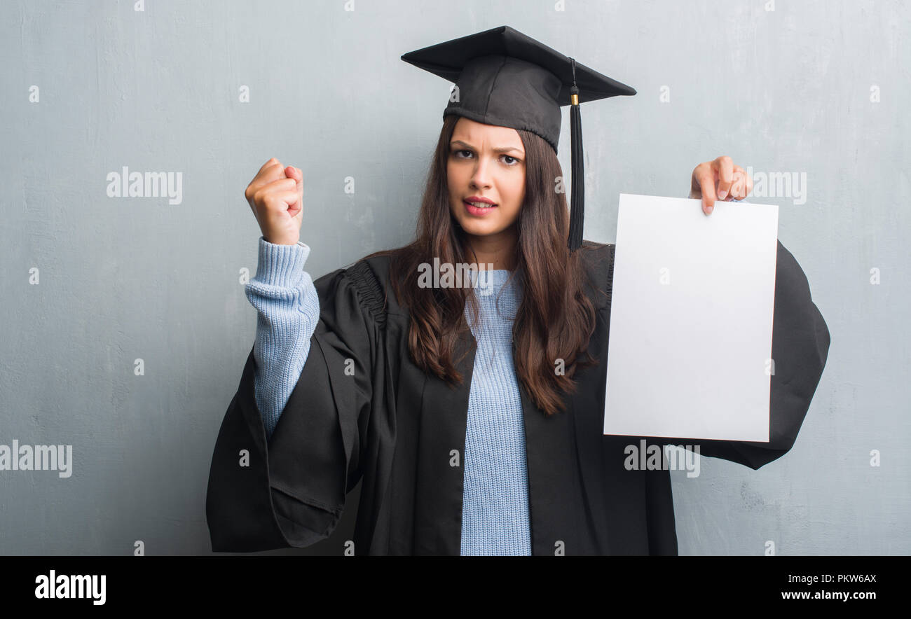 Young brunette woman over grunge grey wall wearing graduate uniform ...