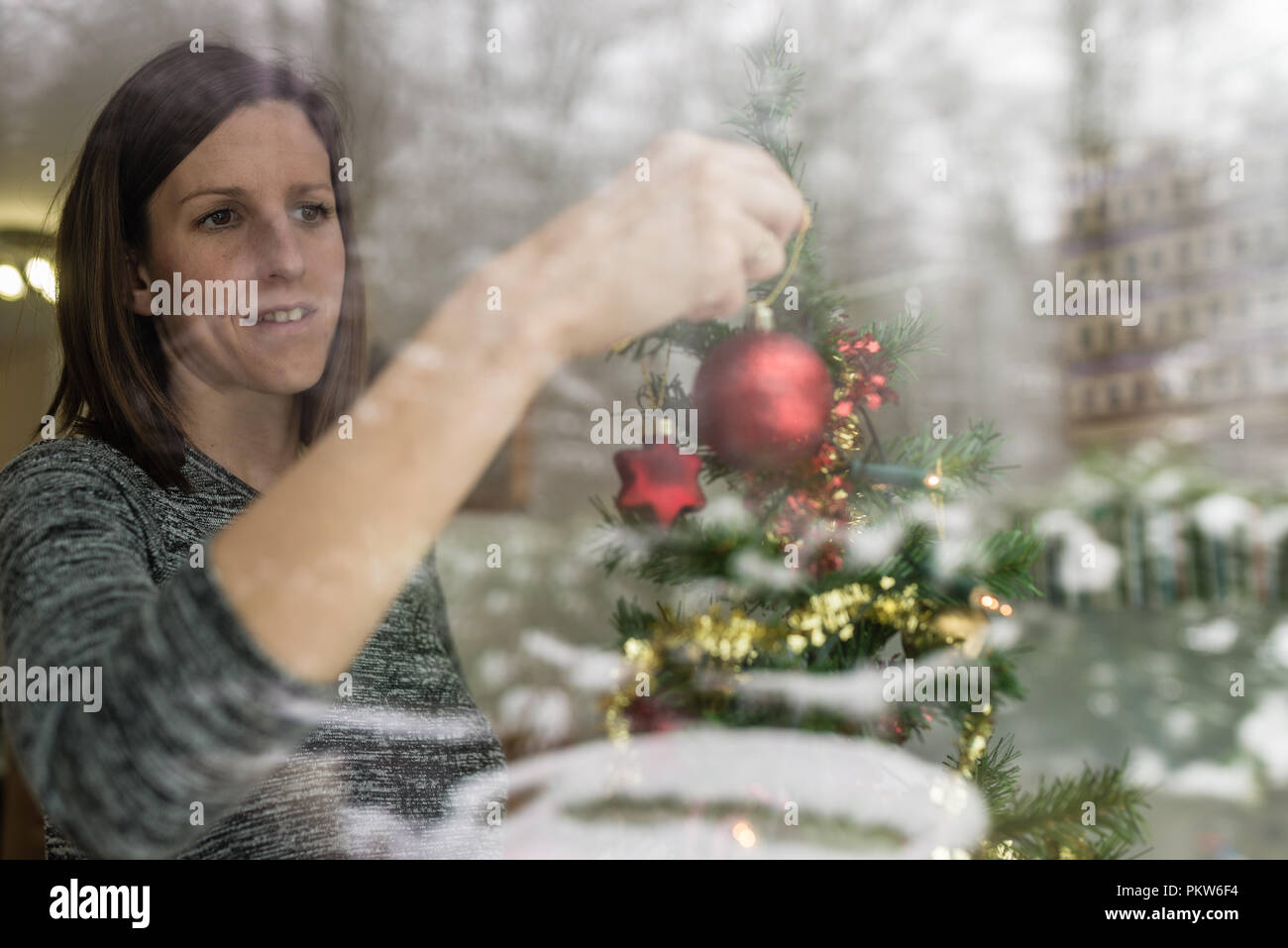 View through a window of a young woman placing red Christmas ball on a ...