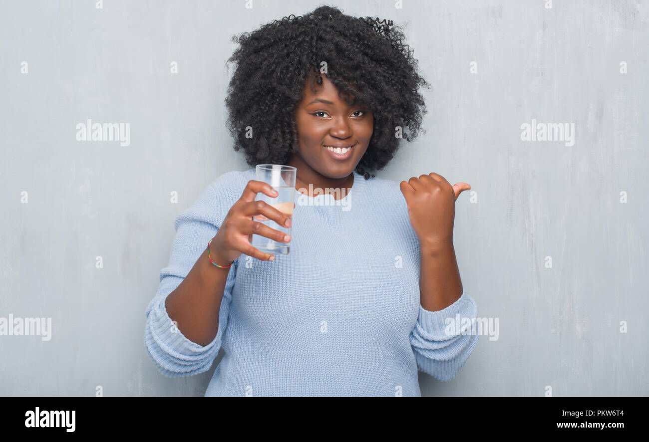 Young african american woman over grey grunge wall drinking a glass of ...