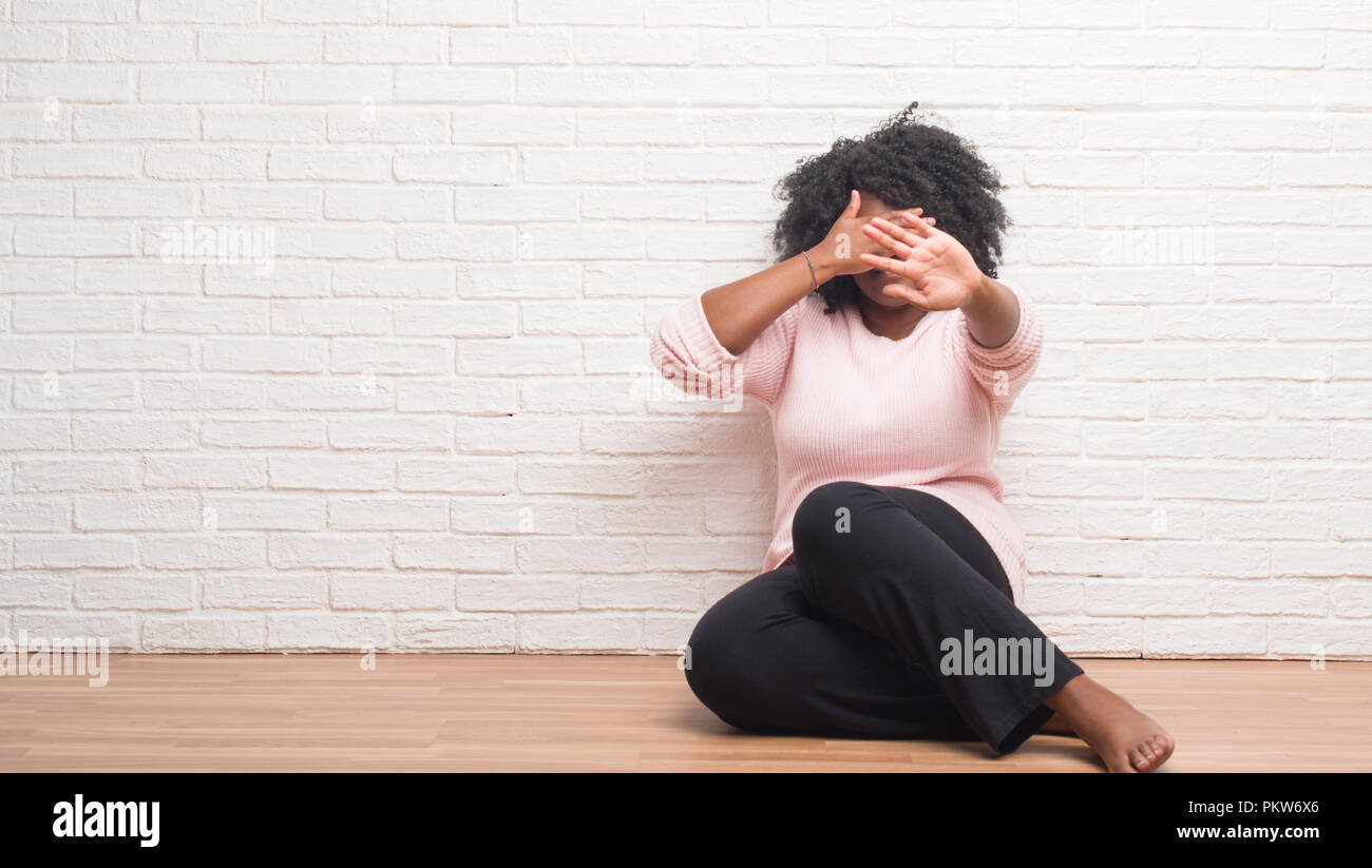 Young african american woman sitting on the floor at home covering eyes ...
